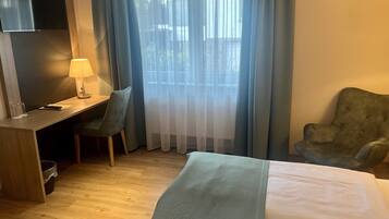 Quarto de hotel com uma cama, uma mesa com abajur, duas cadeiras e uma televisão.