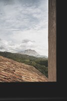 Vista de montanhas por uma janela, com telhado de terracota e colinas verdes exuberantes.