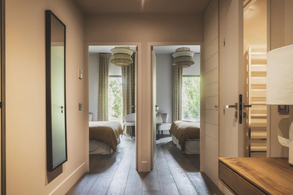 Quarto de hotel com piso de madeira, uma escrivaninha, duas camas e um espelho grande.