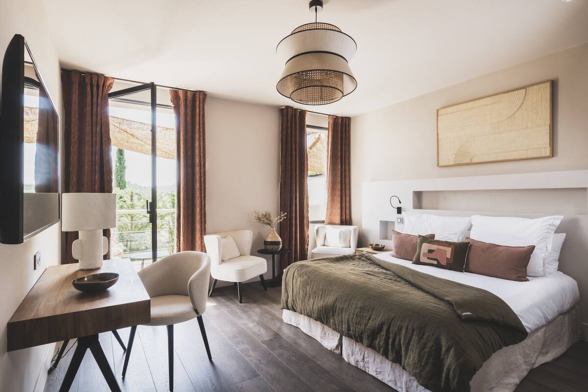 Quarto de hotel moderno com uma cama grande, uma escrivaninha com cadeira, uma televisão e vista para o exterior.
