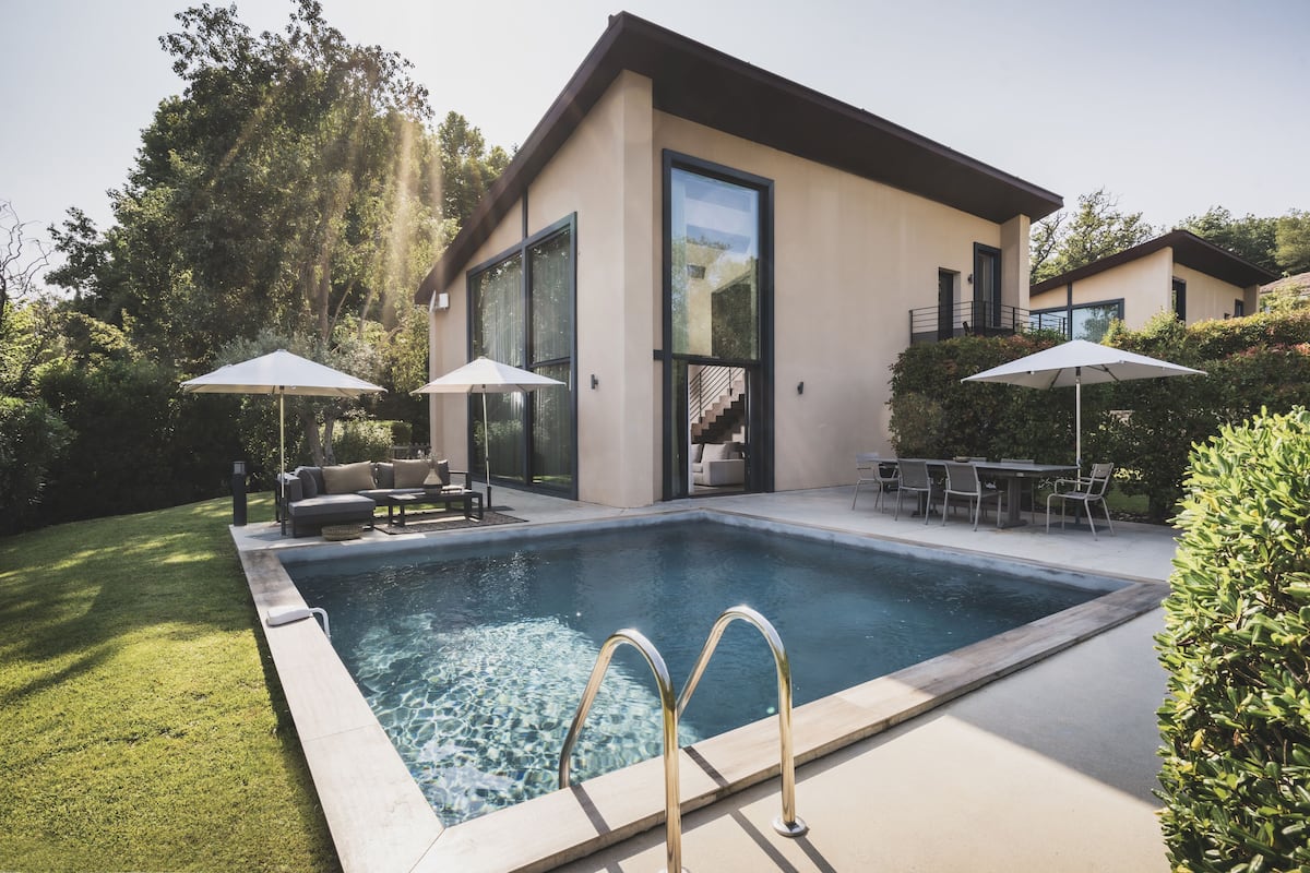 Uma casa moderna com piscina, mobiliário de exterior e grandes janelas.