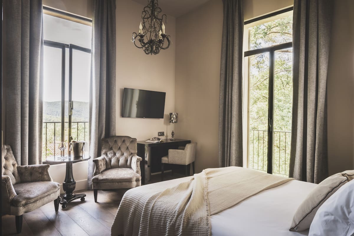 Quarto com uma cama grande, duas poltronas, uma escrivaninha e um candelabro.