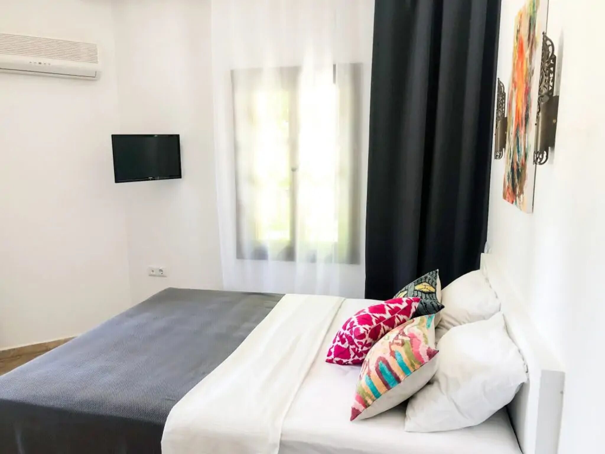 Quarto com cama, televisão de tela plana, janela com cortinas e ar-condicionado fixado na parede.