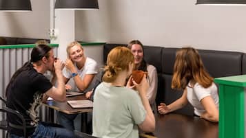 Um grupo de pessoas sentadas à volta de uma mesa num café, com cadeiras pretas e detalhes em verde.