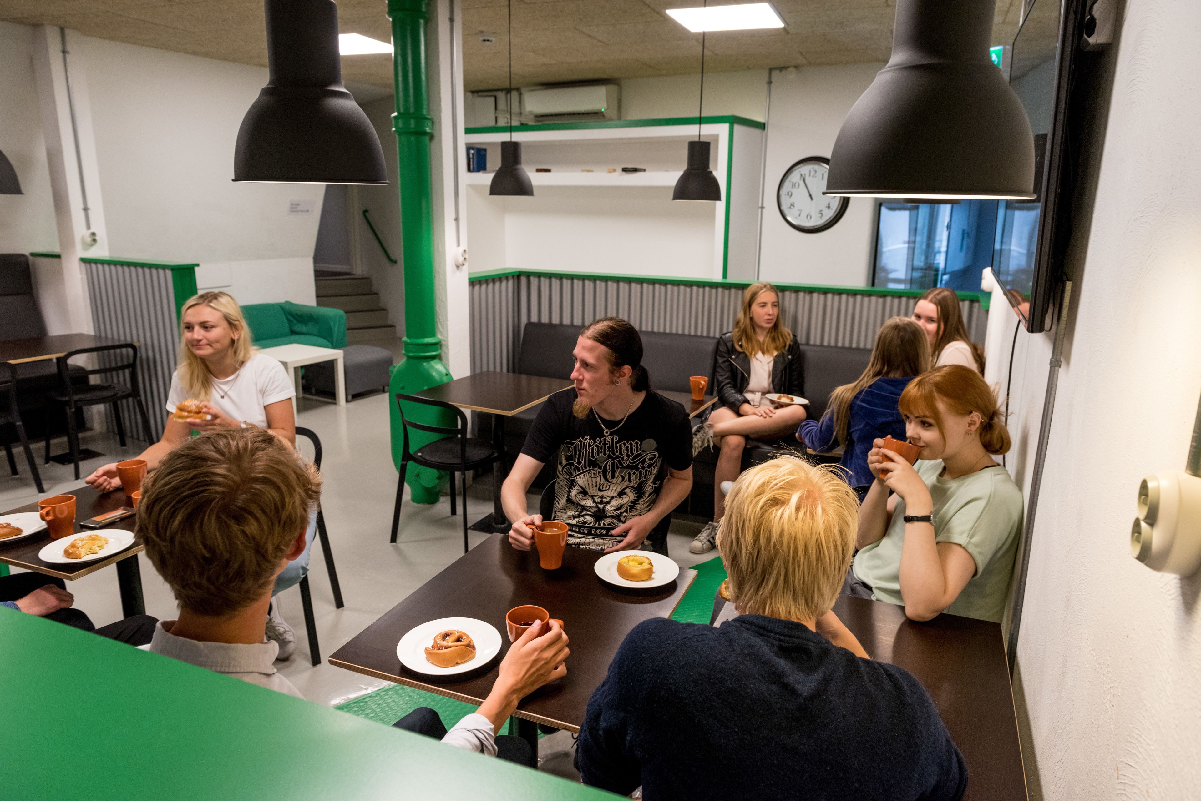Espaço de refeições informal com mesas, cadeiras e pessoas a comer.