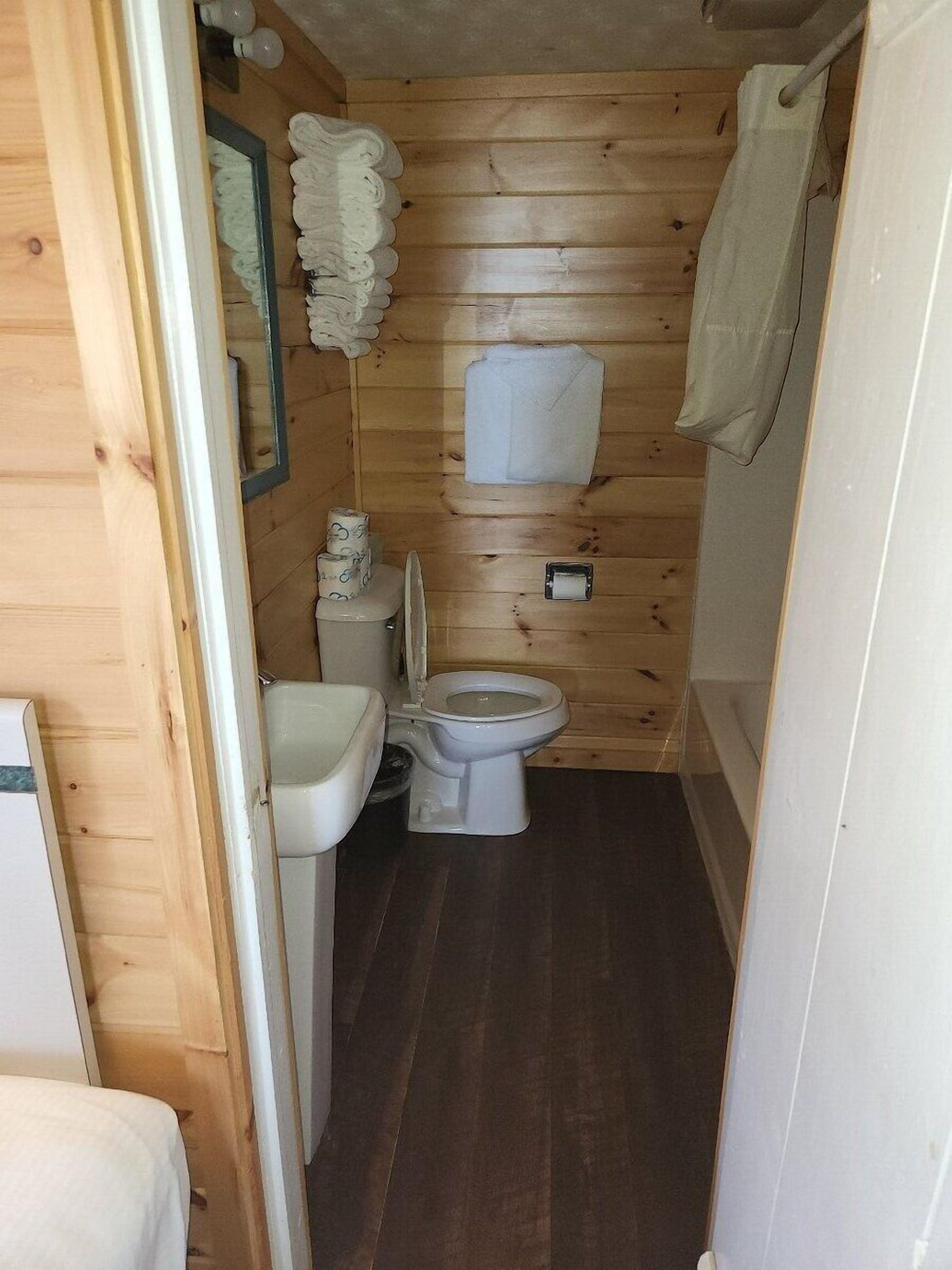 Casa de banho de uma cabana de madeira pequena, com sanita, lavatório e suporte para toalhas.