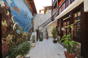 Um pátio com um mural de vida marinha, degraus de pedra, plantas em vasos e varandas de madeira tradicional.