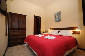 Quarto de hotel com uma cama grande, um guarda-roupa de madeira, um quadro na parede e uma televisão fixada na parede.