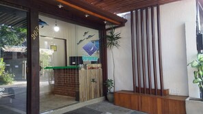 Uma área de recepção com porta de vidro, cerca de bambu e uma placa com a inscrição 'Pousada VerdeMar'.