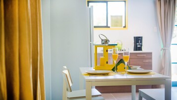 Uma área de refeições com uma mesa posta para dois, um abajur amarelo e uma janela com cortinas.