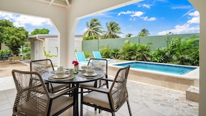 Um pátio externo com piscina, cadeiras de vime e uma mesa posta para refeições.