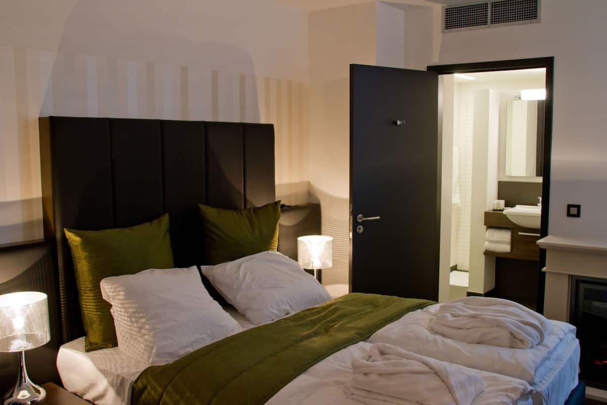 Quarto de hotel com cama, abajures, porta, espelho e lareira.