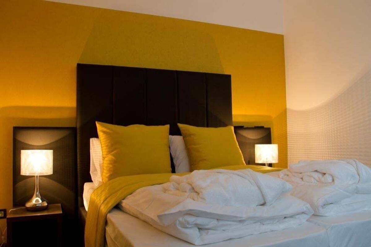 Quarto de hotel com uma cama, duas luminárias de cabeceira e um painel de cabeceira.