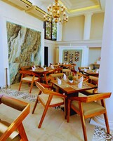 Uma área de jantar com mesas e cadeiras de madeira, um candelabro e uma parede com garrafas de vinho.