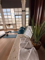 Quarto com tapetes de exercício, um rolo de yoga, uma planta em vaso e um certificado emoldurado sobre uma mesa.
