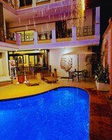 Uma área de piscina interior com vários níveis, piscina central, espreguiçadeiras e mesas.