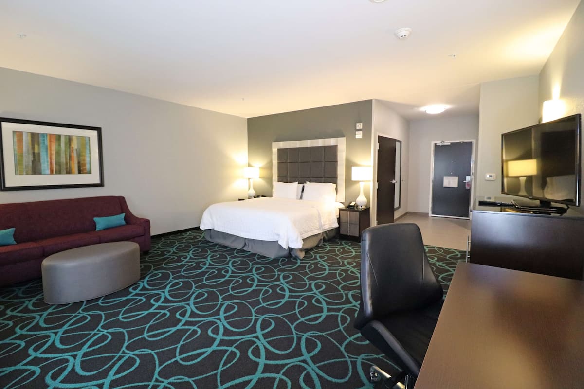 Quarto de hotel com cama, sofá, escrivaninha e televisão.