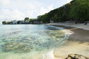 Uma praia com águas cristalinas, areal dourado e edifícios ao fundo.