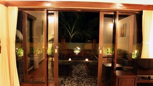 Entrada por porta de vidro deslizante para um quarto com uma pequena mesa e cadeiras, um caminho de pedrinhas e um vaso de planta.