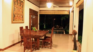 Uma área de refeições com mesa e cadeiras de madeira, um ventilador de teto e um quadro decorativo na parede.