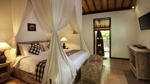 Quarto com cama de dossel, luminárias de cabeceira, mesa de cabeceira de madeira, um banco, armário de madeira e uma televisão na parede.