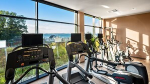 Uma academia com equipamentos de cardio, janelas amplas e vista para o mar.