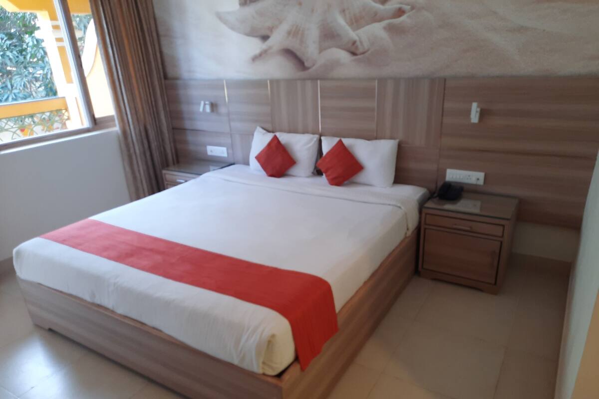 Quarto de hotel com uma cama grande, mesa de cabeceira, abajur e vista para o exterior.