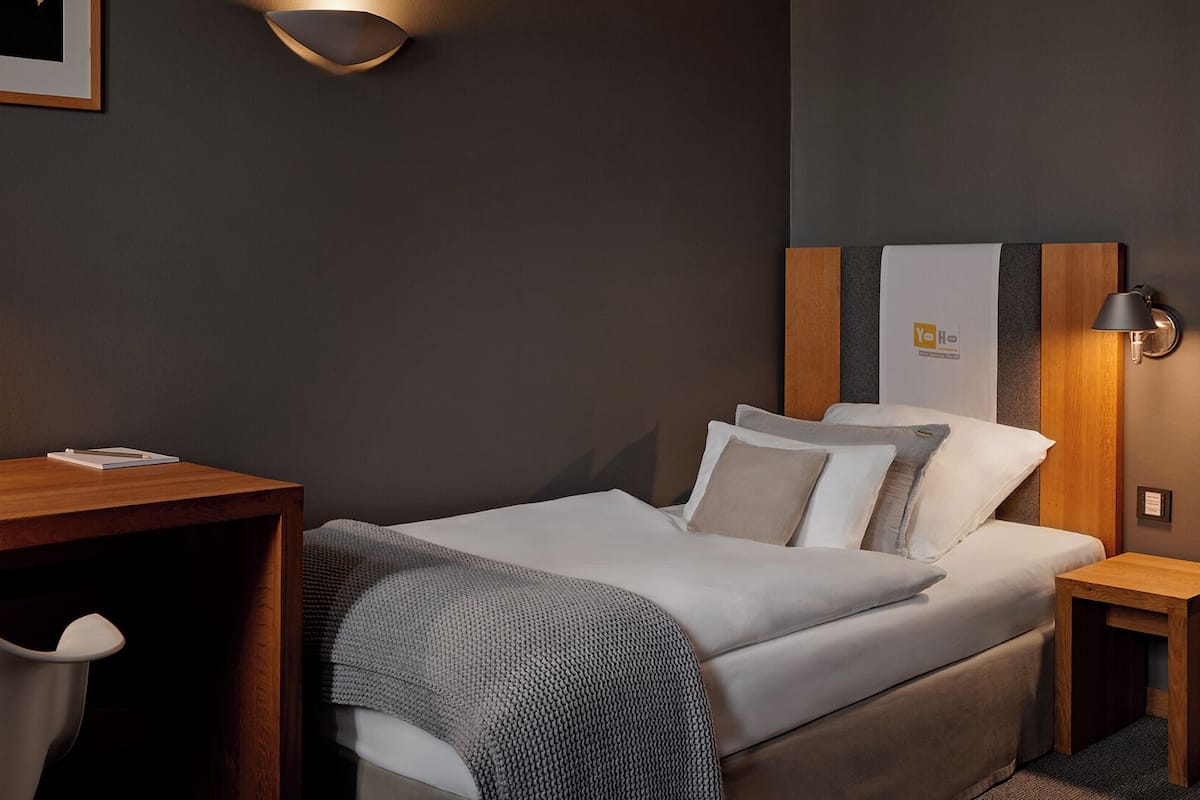 Quarto de hotel com cama, mesa de cabeceira, abajur e quadro na parede.