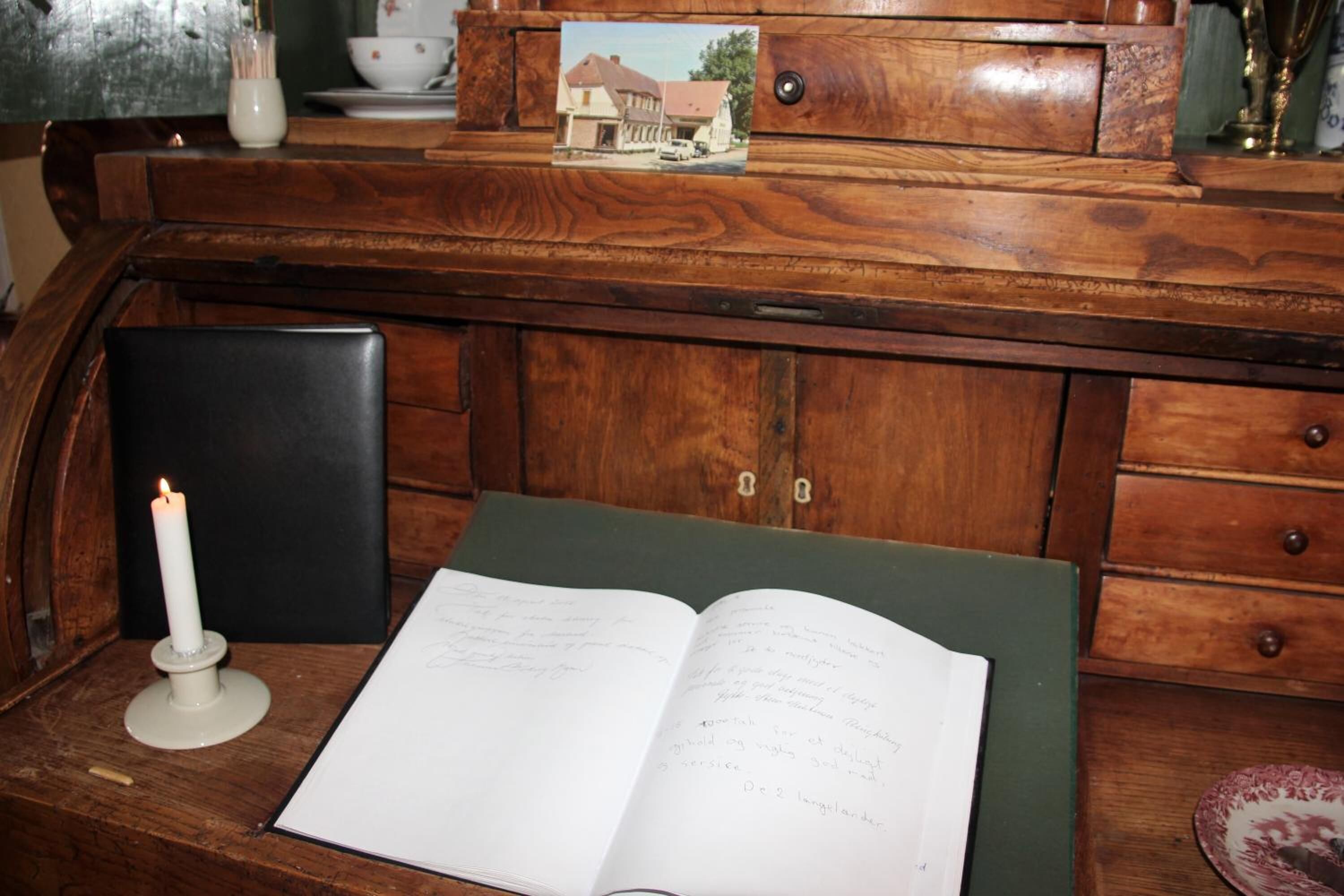 Uma mesa de madeira com um livro, uma vela e uma pequena fotografia.