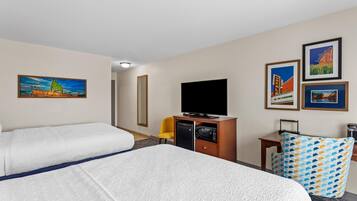 Quarto de hotel com duas camas, televisão, micro-ondas e obras de arte nas paredes.