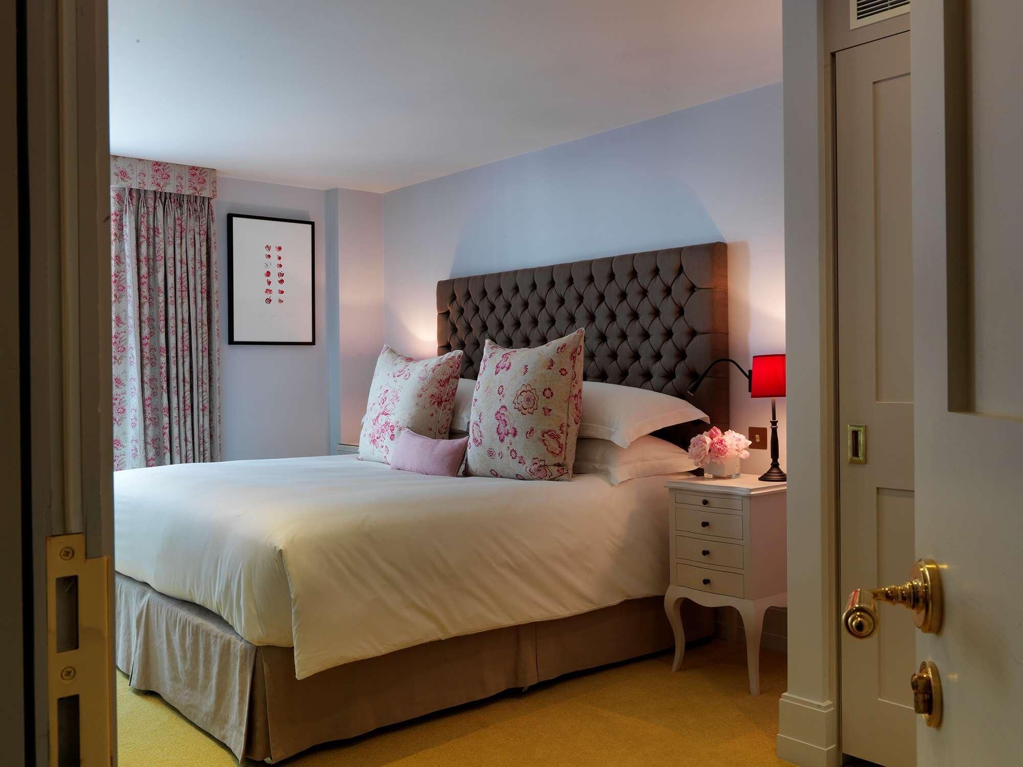 Um quarto com uma cama grande, uma mesa de cabeceira com luminária e uma porta com puxador de latão.