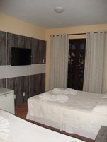 Quarto de hotel com uma cama, televisão fixada na parede e uma kitchenette pequena.