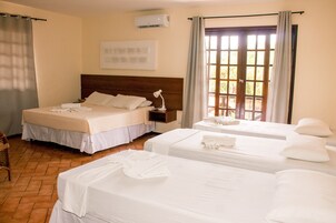 Quarto de hotel com duas camas, cabeceira de madeira, mesa de cabeceira, abajur e janela com cortinas.