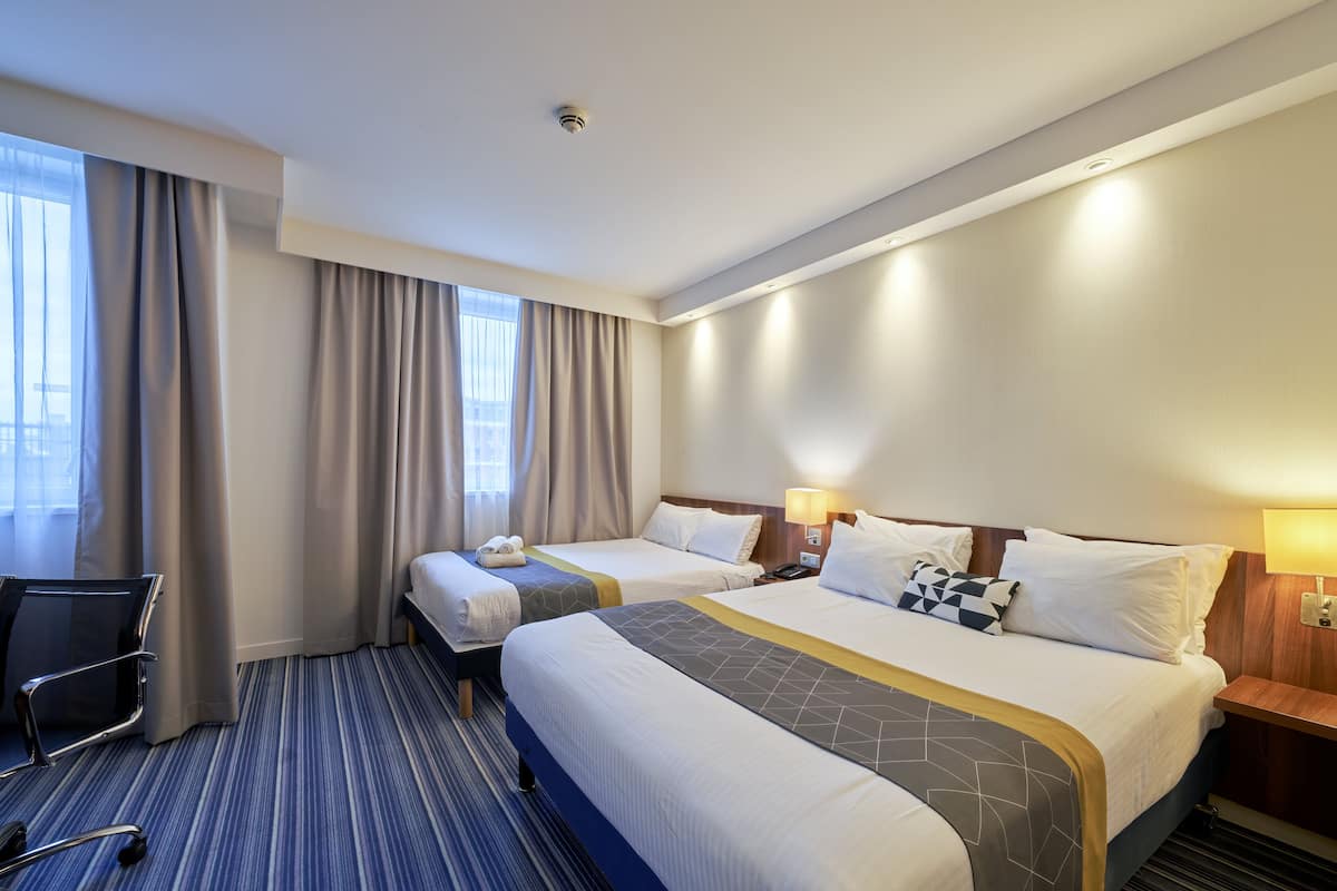 Quarto de hotel com duas camas, uma mesa, uma cadeira e uma janela com cortinas.