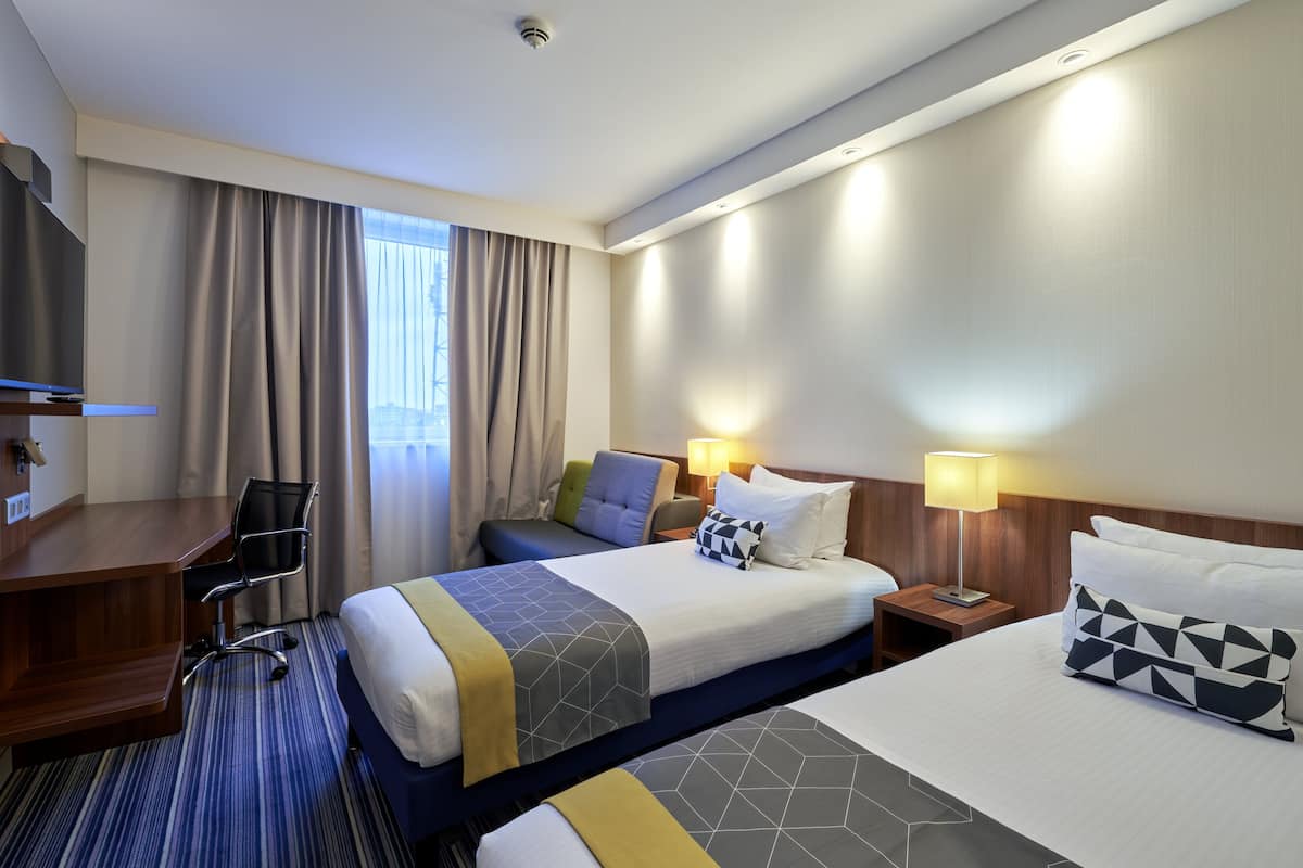 Quarto de hotel com duas camas, uma escrivaninha, uma cadeira e uma televisão.