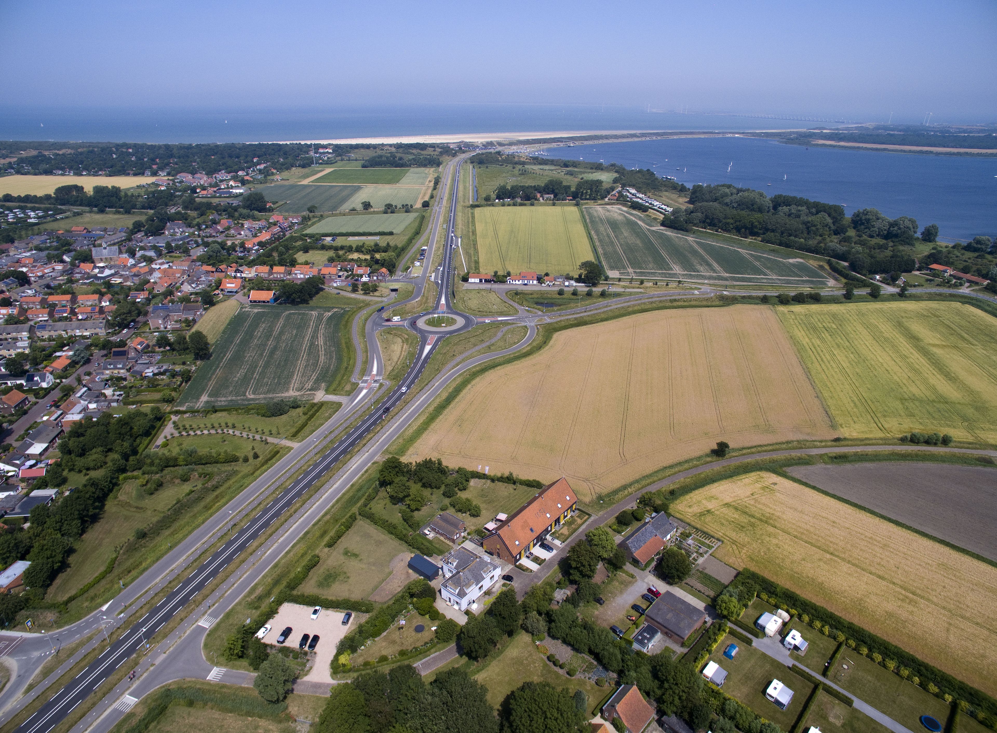 Vista aérea de uma cidade com uma rotatória, estradas, campos e uma ponte ao longe.