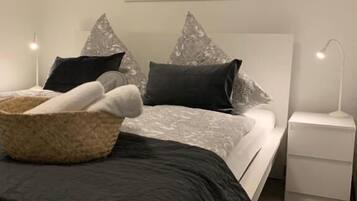 Quarto bem arrumado com cama, almofadas, mesa de cabeceira e luminária na parede.