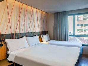Quarto de hotel com duas camas, uma janela grande e vista para a cidade.