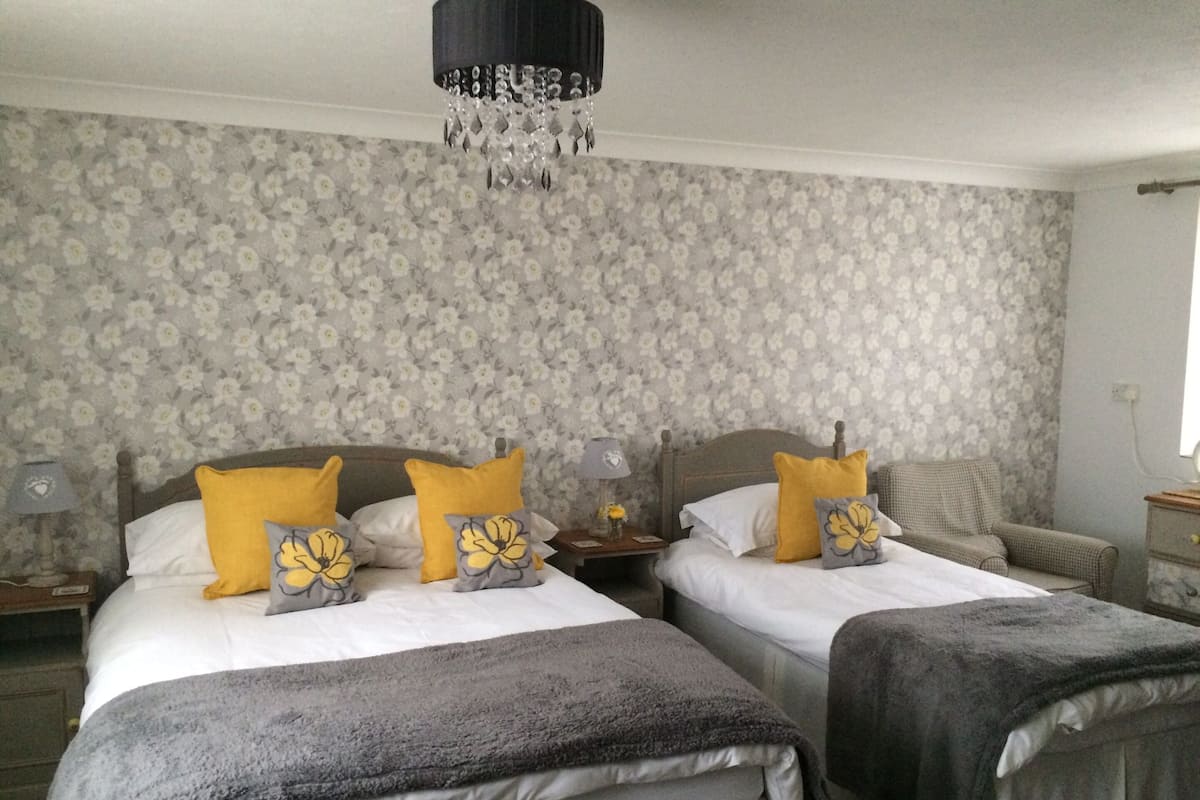 Quarto duplo com duas camas, papel de parede floral, um candelabro e uma mesa de cabeceira com abajur.