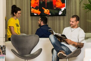 Quarto com sofá, cadeira, televisão e revista no chão.