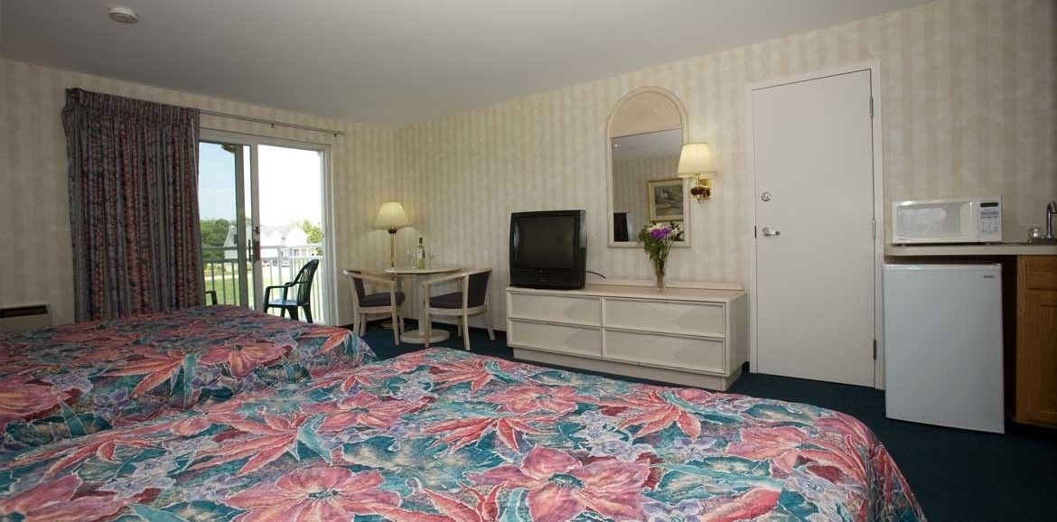 Quarto de hotel com uma cama grande, uma mesa com cadeira, televisão, micro-ondas e frigorífico.