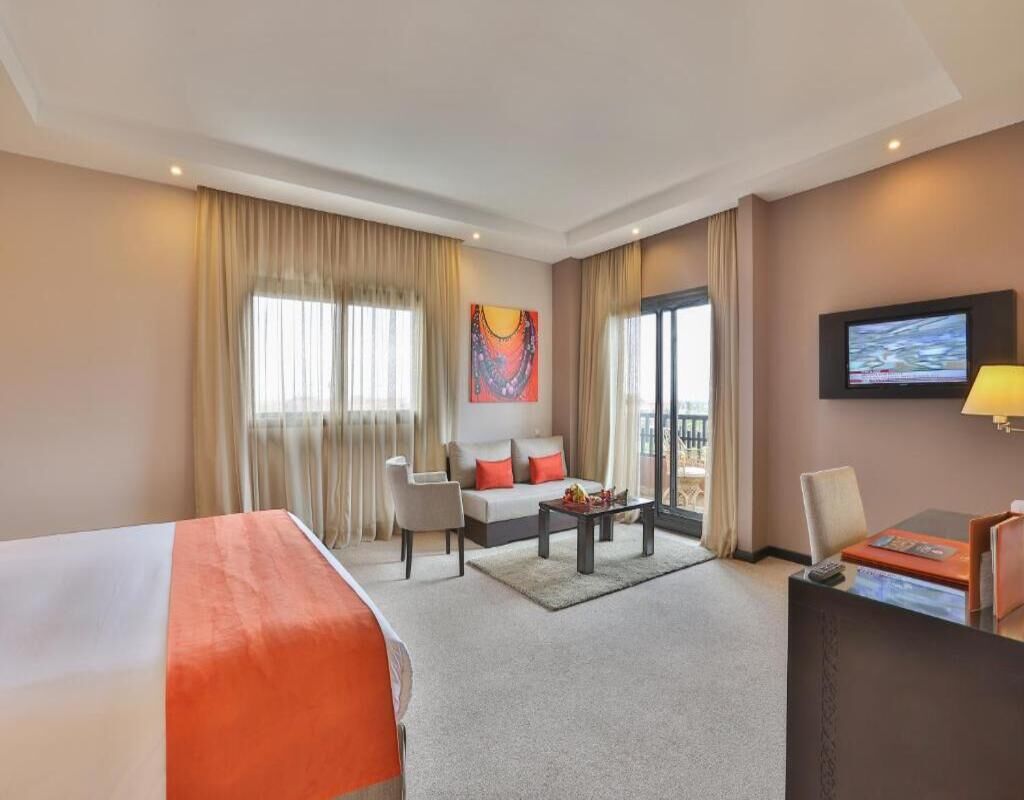 Quarto de hotel com cama, sofá, mesa de centro, escrivaninha e televisão.