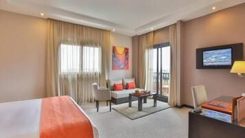Quarto de hotel com cama, sofá, mesa de centro, escrivaninha e televisão.
