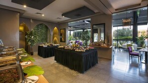 Buffet com diversos alimentos, área de estar com mesas e cadeiras, e vista para o verde lá fora.