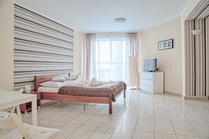Quarto de hotel moderno com cama, mesa de cabeceira, televisão e vista para a cidade pela janela.