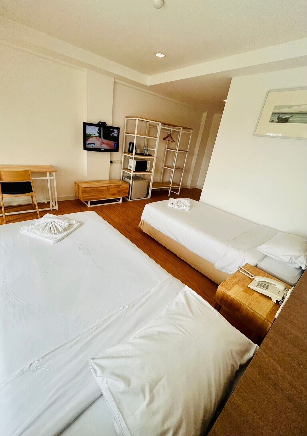 Quarto de hotel com duas camas, uma escrivaninha, televisão, guarda-roupa e um quadro pendurado na parede.