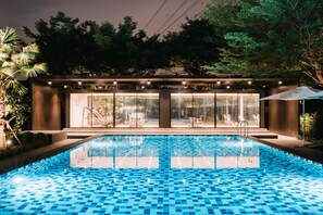 Piscina com piso revestido, rodeada por um edifício com amplas janelas de vidro e área externa coberta.
