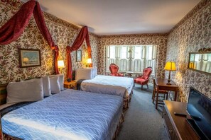 Quarto de hotel com duas camas, uma escrivaninha, uma cadeira, uma televisão e uma janela com persianas.