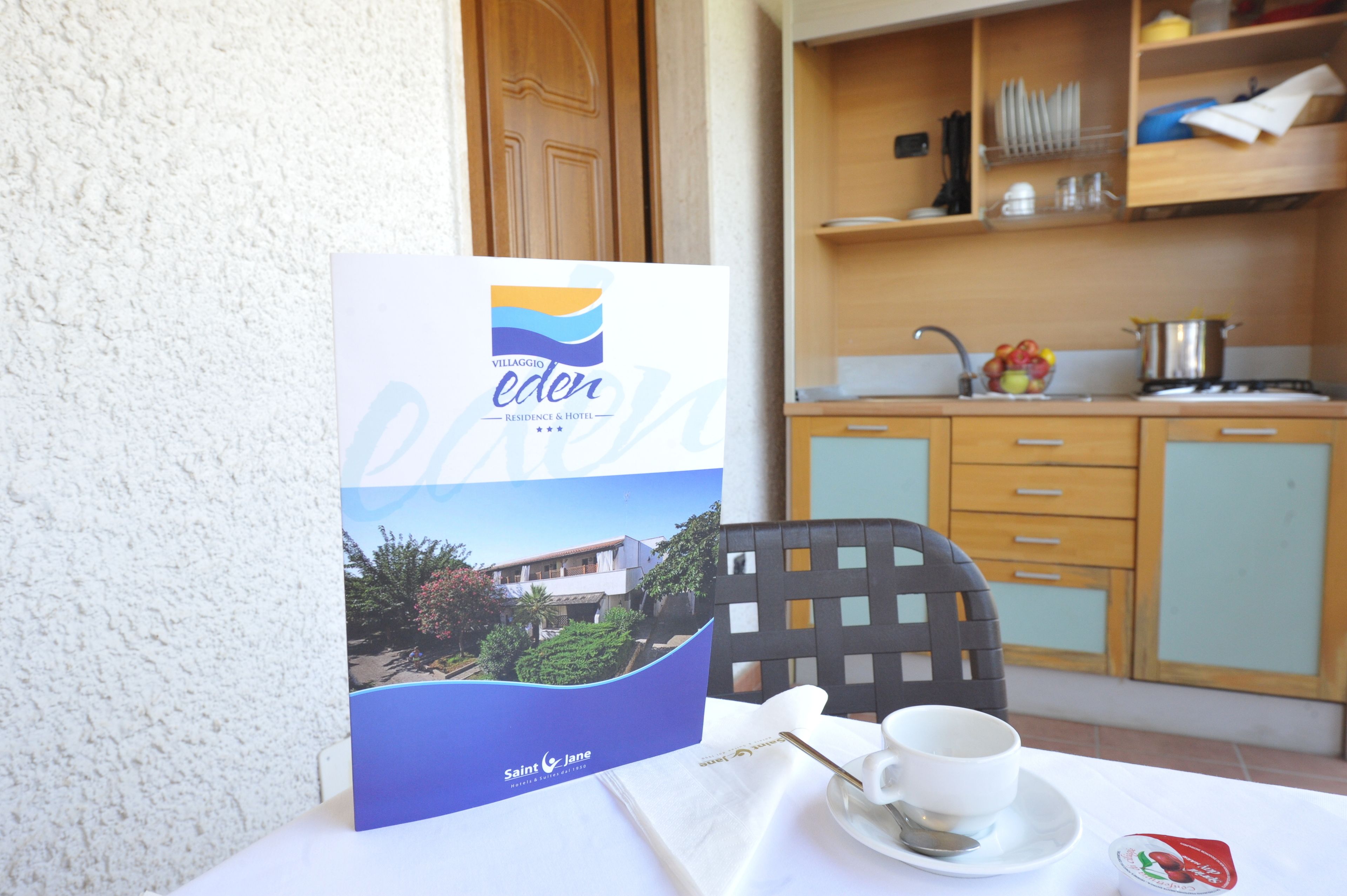 Um folheto do Saint Jane Eden Residence & Hotel, com uma área de cozinha, armários de madeira, uma pia e uma fruteira.