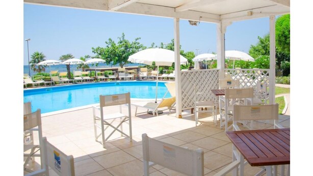 Uma área à beira da piscina com espreguiçadeiras e guarda-sóis, piscina e vista para o mar.